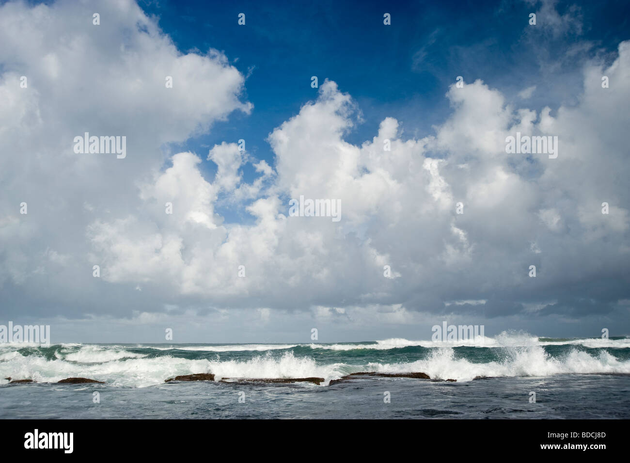 Waves breaking against a rock reef with cumulus clouds building in the ...