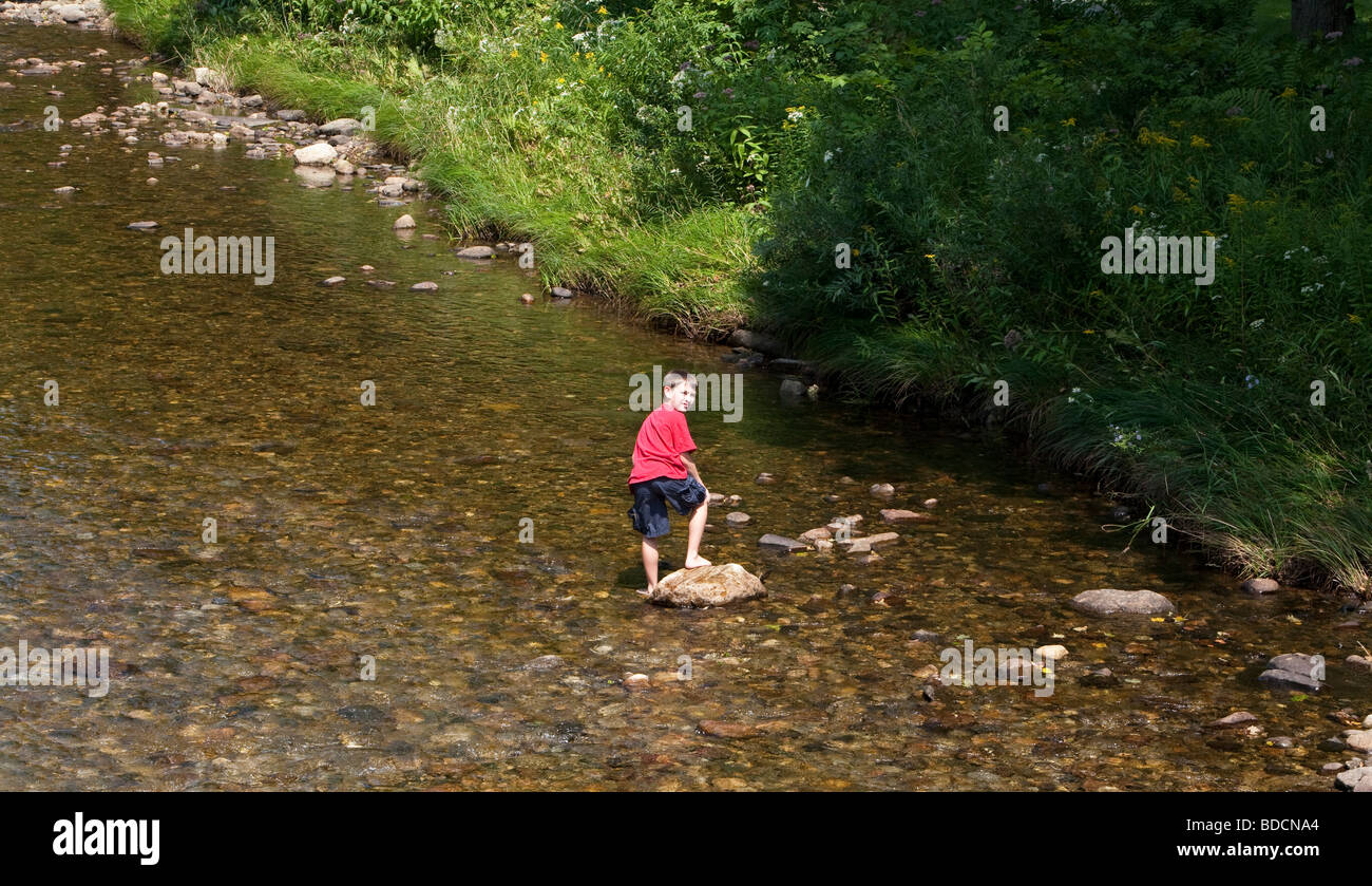 A young boy wading in a stream in Vermont United States on a hot summer ...