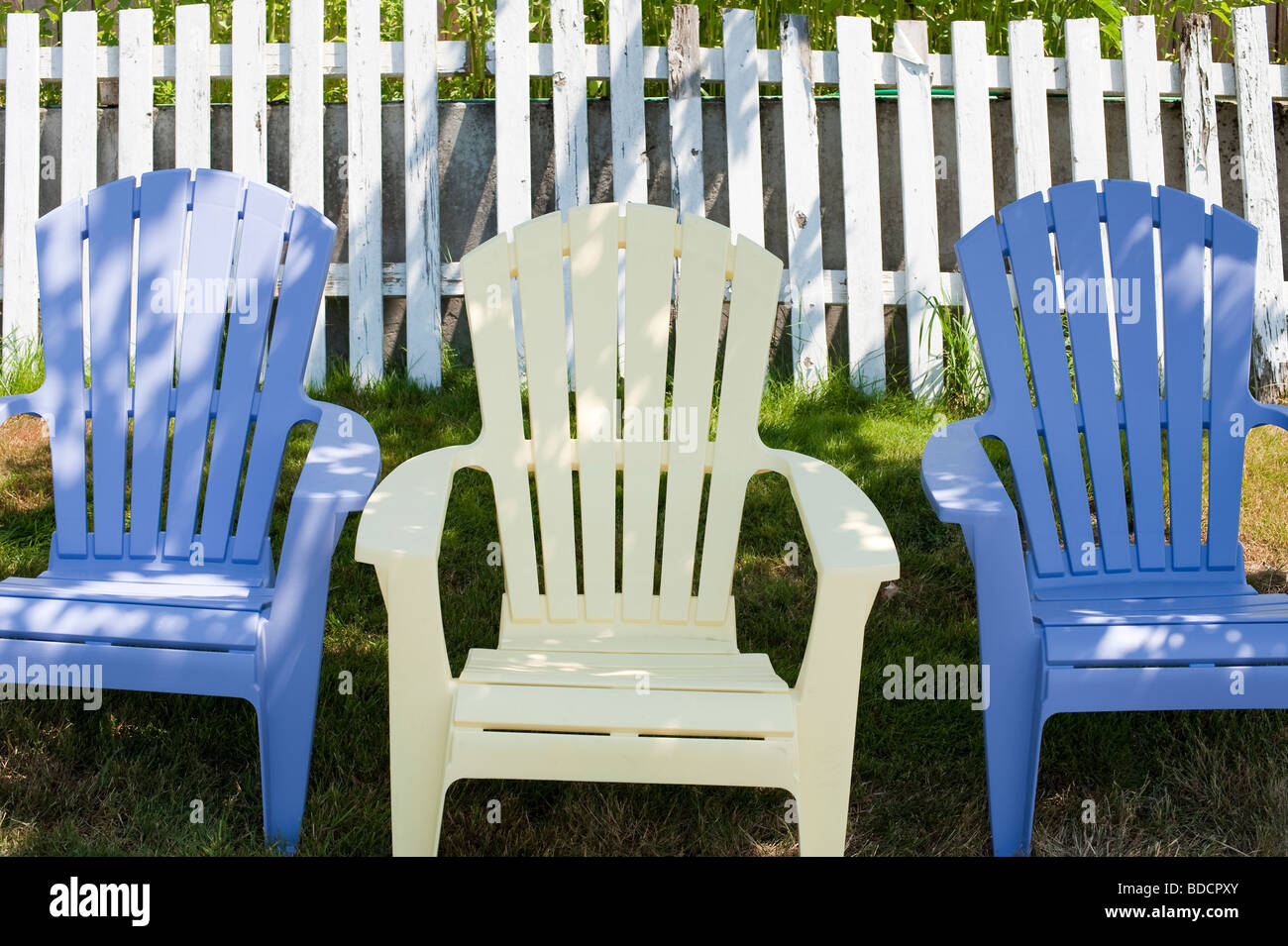 Lawn chairs lined up under the shade of a tree with white picket fence ...