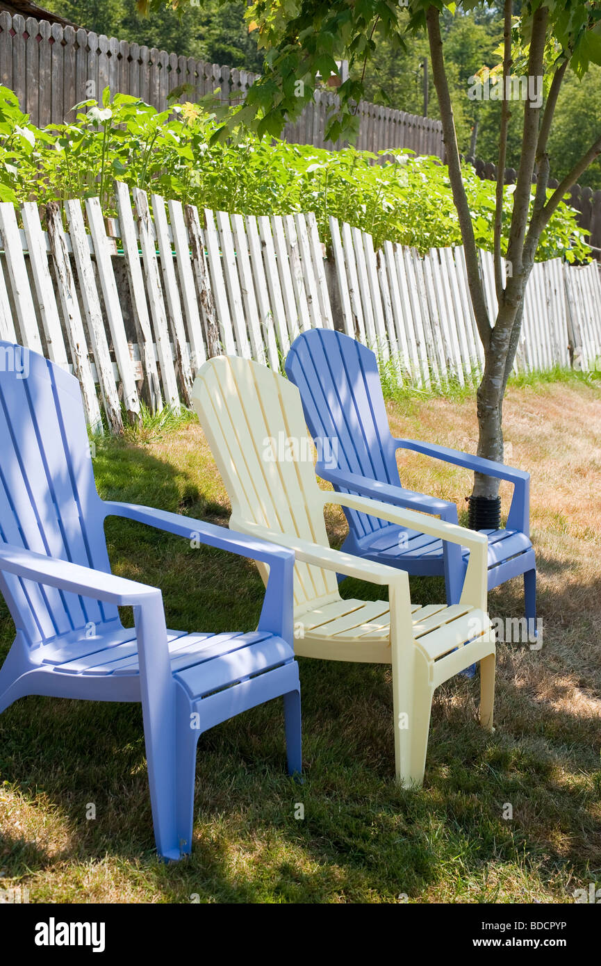 Lawn chairs lined up under the shade of a tree with white picket fence ...
