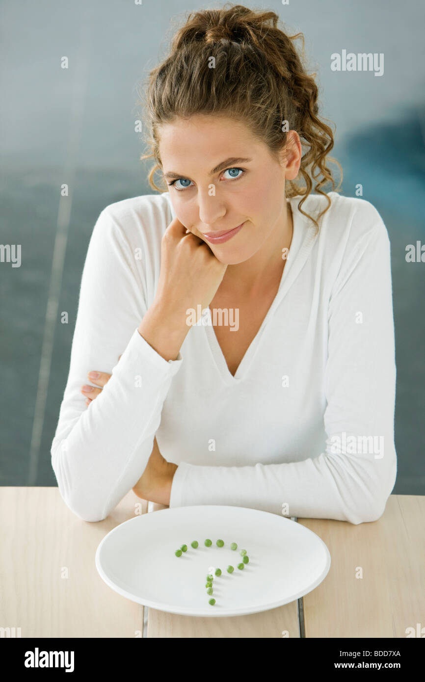 Woman sitting at a table with peas in question mark shape on a plate ...