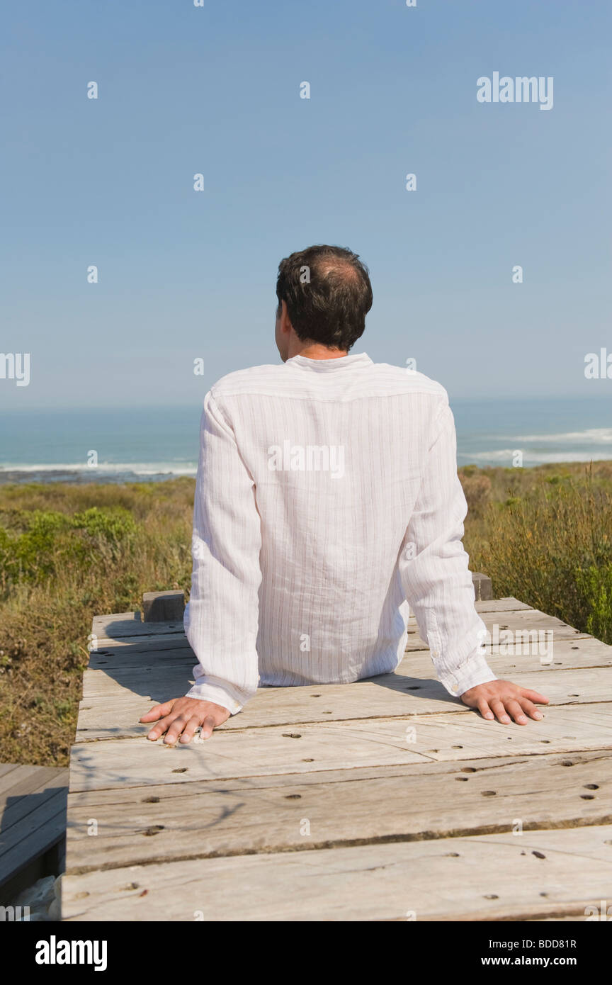 Rear view of a man sitting on a boardwalk Stock Photo - Alamy