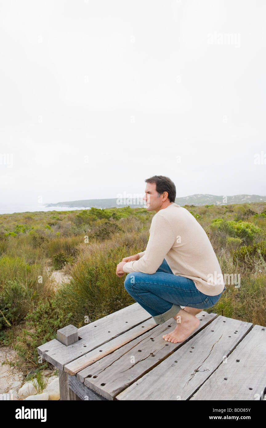 Man crouching on a boardwalk and thinking Stock Photo - Alamy