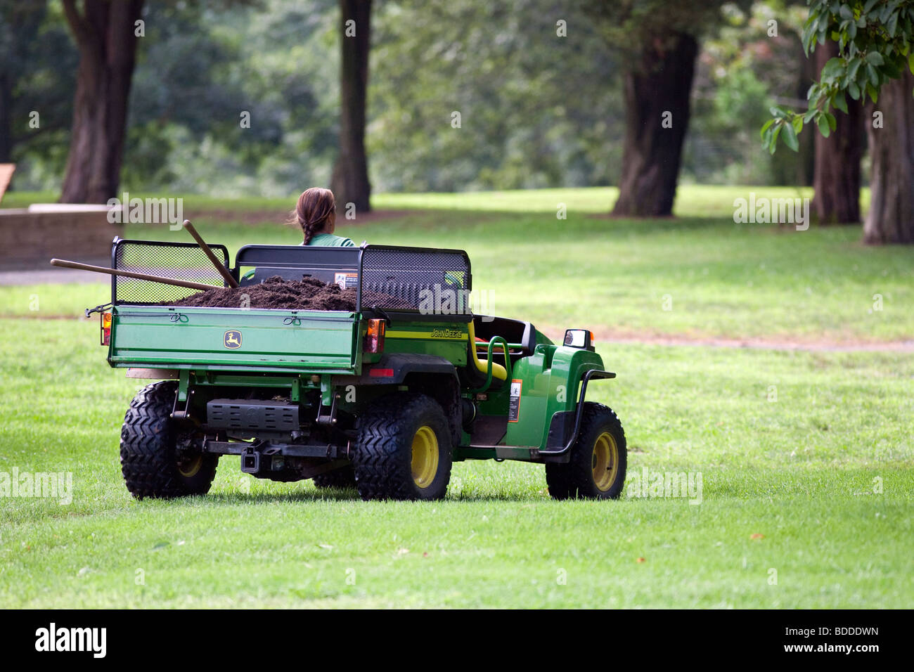 Carrying mulch in a John Deere utility vehicle. A female gardener is ...
