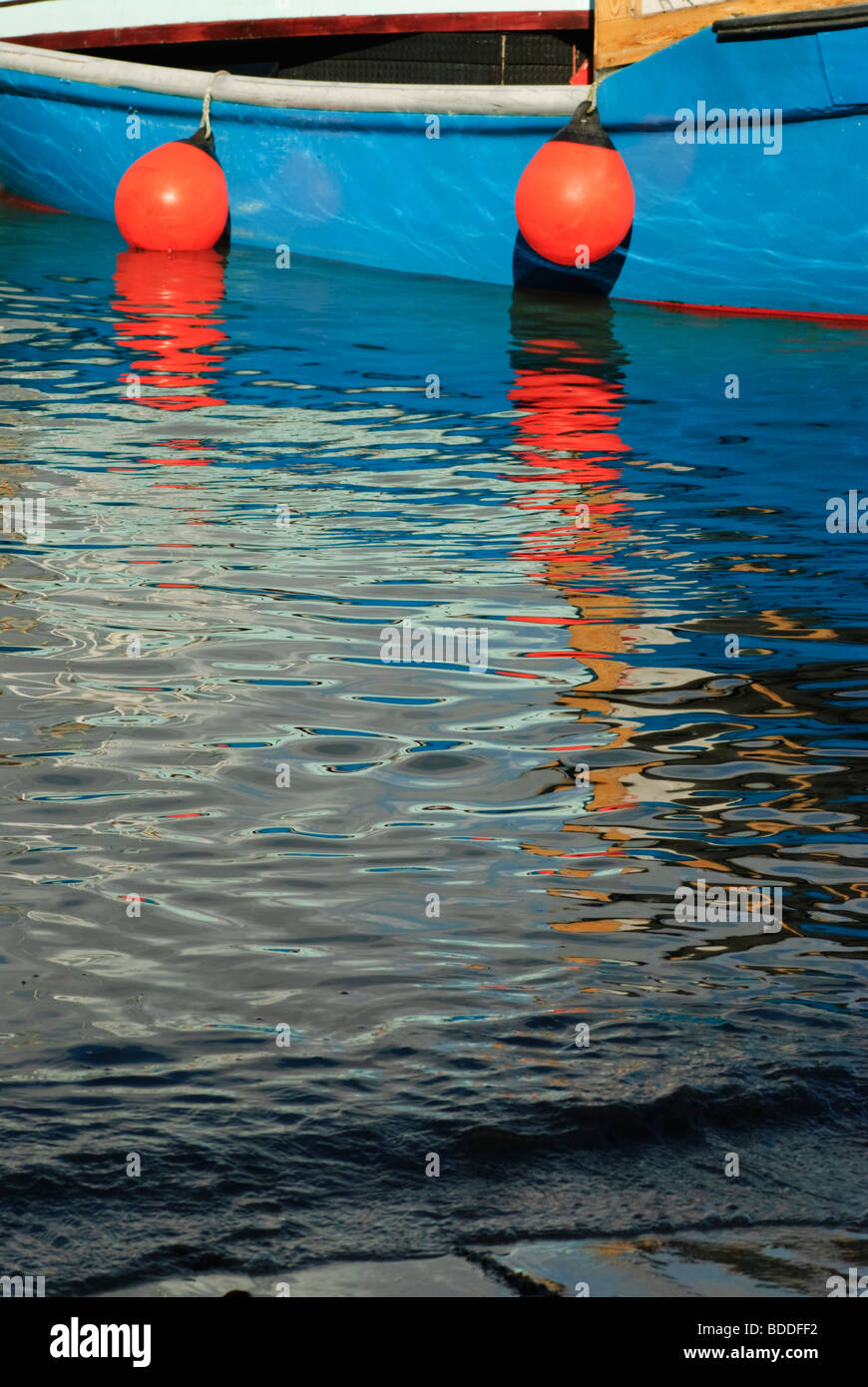 Two red buoys and a blue fishing boat are reflected in the sea Stock ...