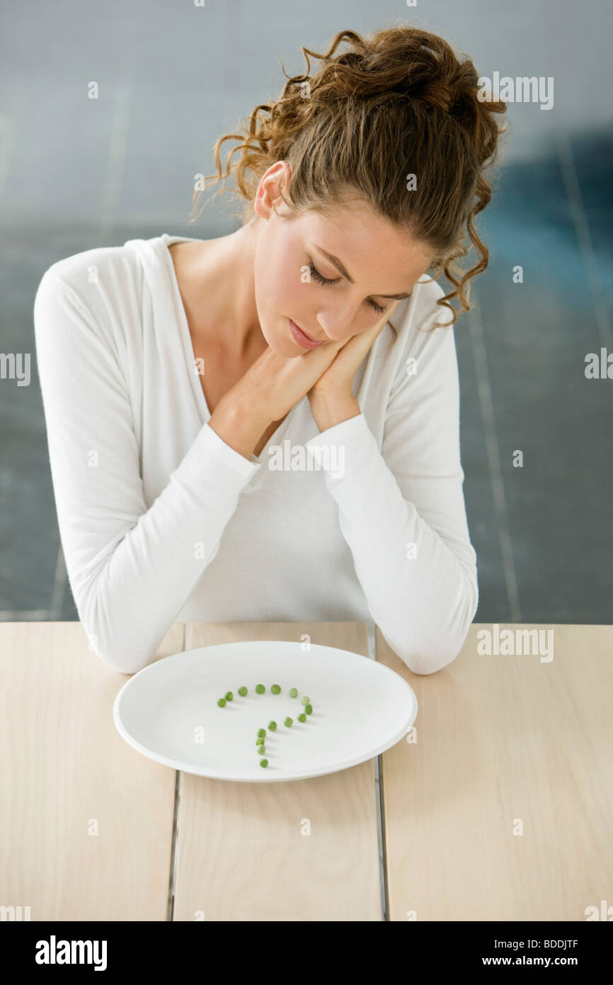 Woman sitting at a table with peas in question mark shape on a plate ...