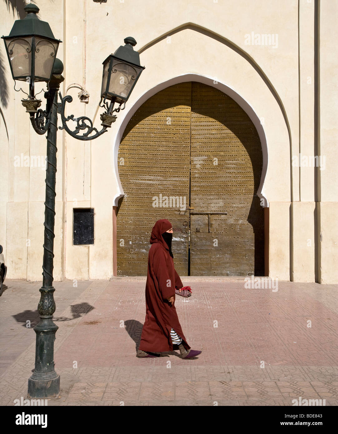 A woman in traditional dress passes the key hole arch of the Kasbah ...
