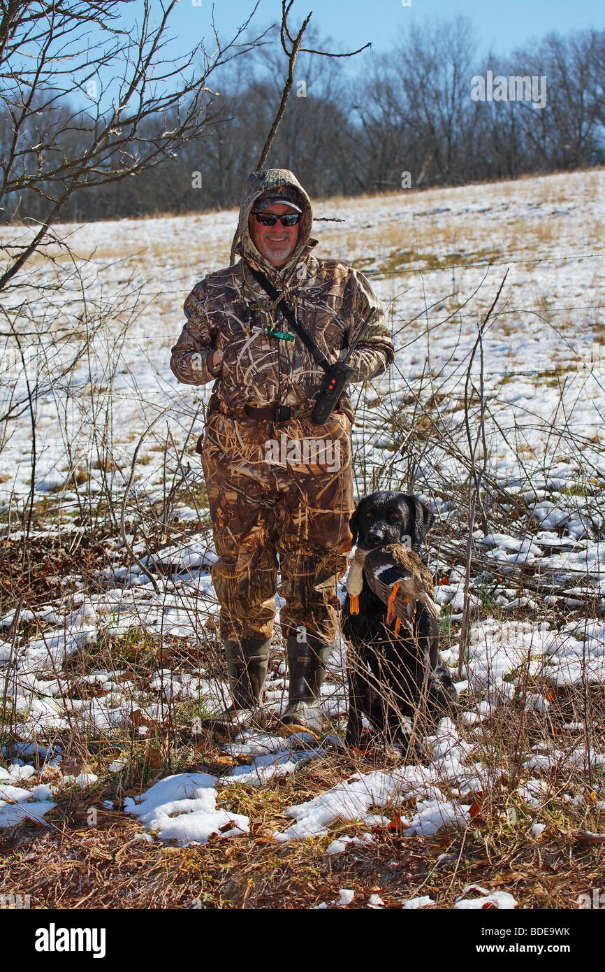 HUNTING GUIDE STANDING WITH BLACK LAB LABRADOR WITH DUCK IN MOUTH COLD ...