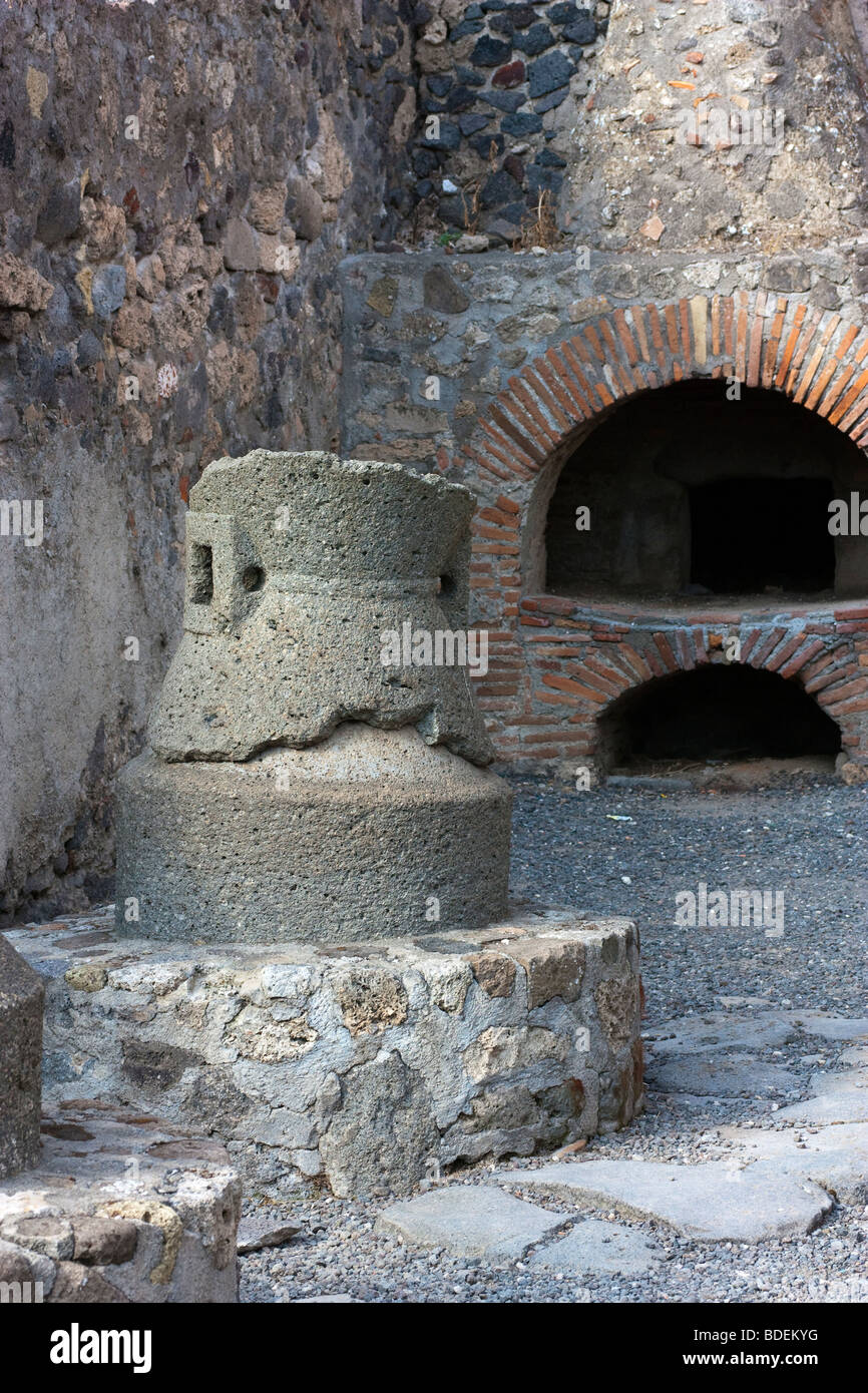An ancient millstone and an oven in the ruins of a bakery at Pompeii ...