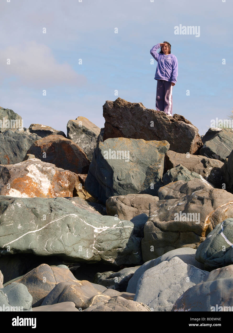 Young girl stood on the top of rocks looking out to sea Stock Photo - Alamy
