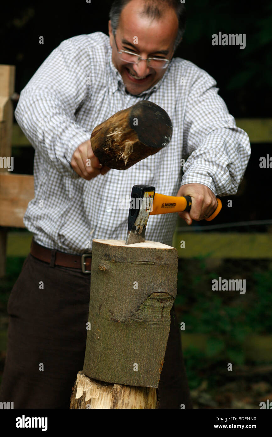 Man enthusiastically using mallet hand to split log by hitting hand axe ...