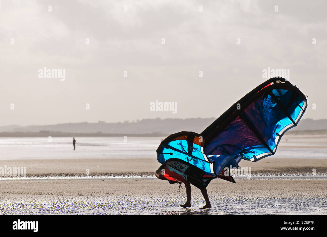 A parasurfer carrying his equipment along the beach at Camber Sands in ...