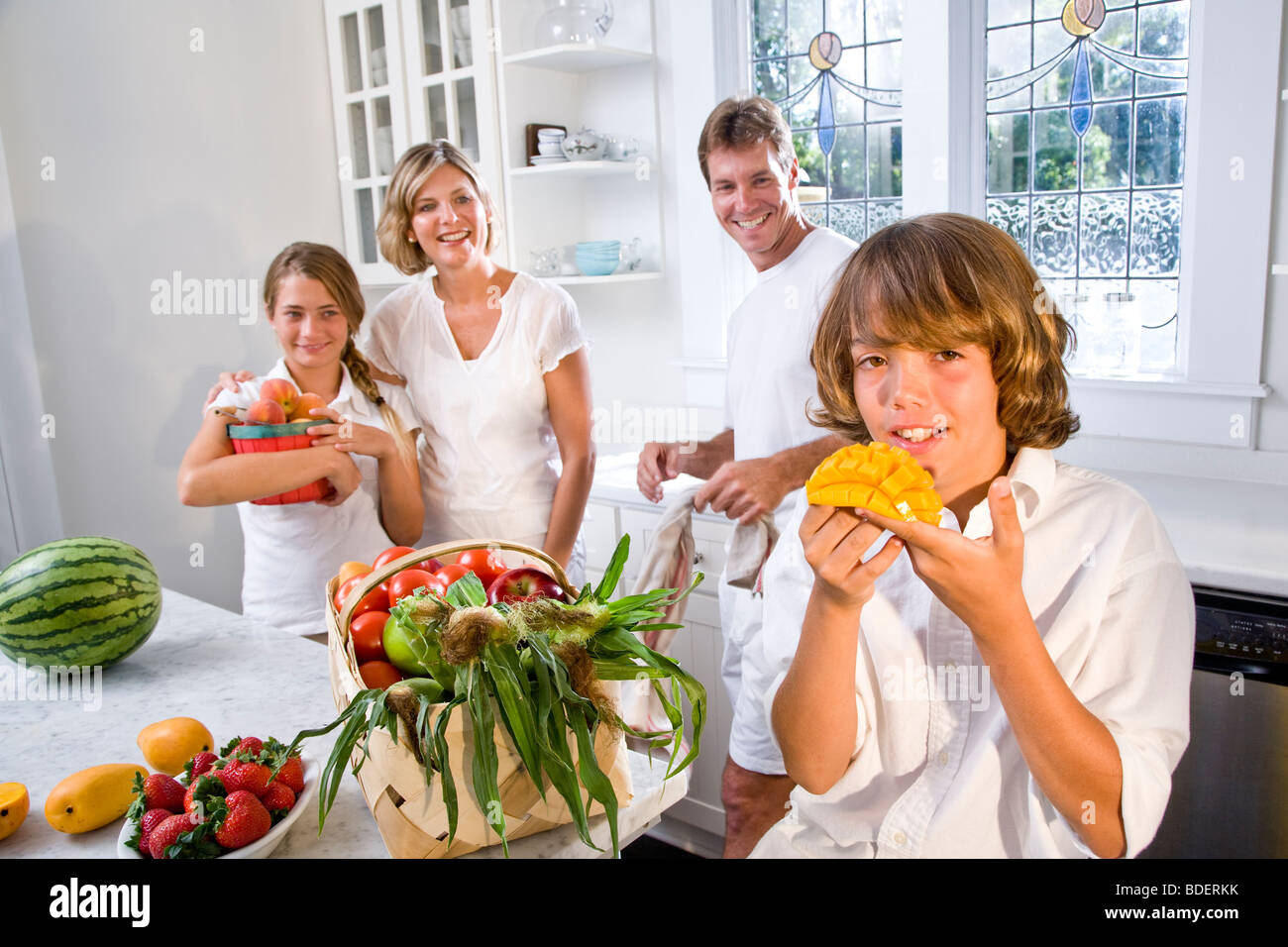 Boy eating mango in kitchen with family standing behind Stock Photo - Alamy