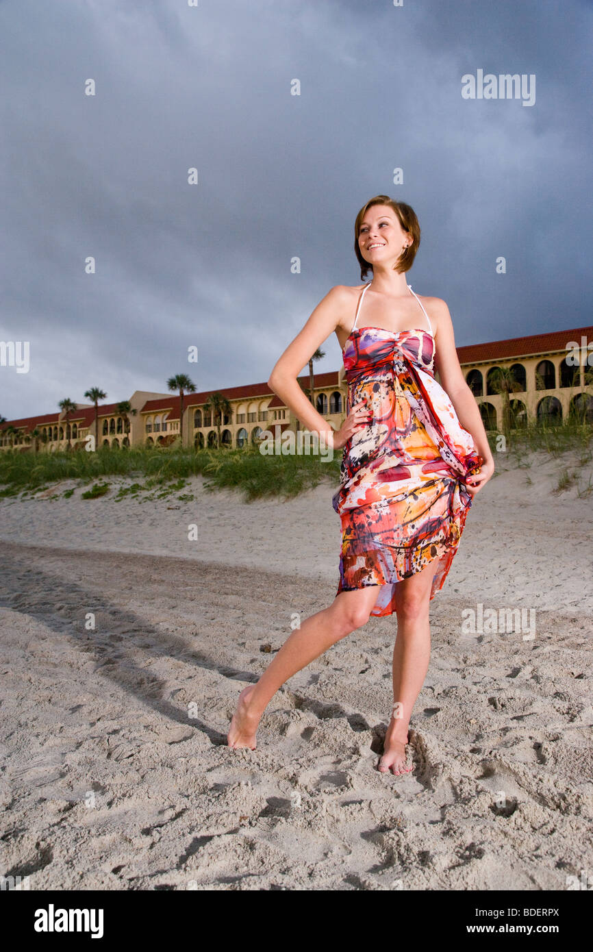 Young woman in colorful sundress standing on beach in front of resort ...