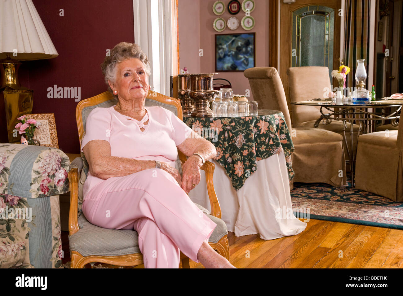 Elderly woman sitting on living room chair Stock Photo - Alamy
