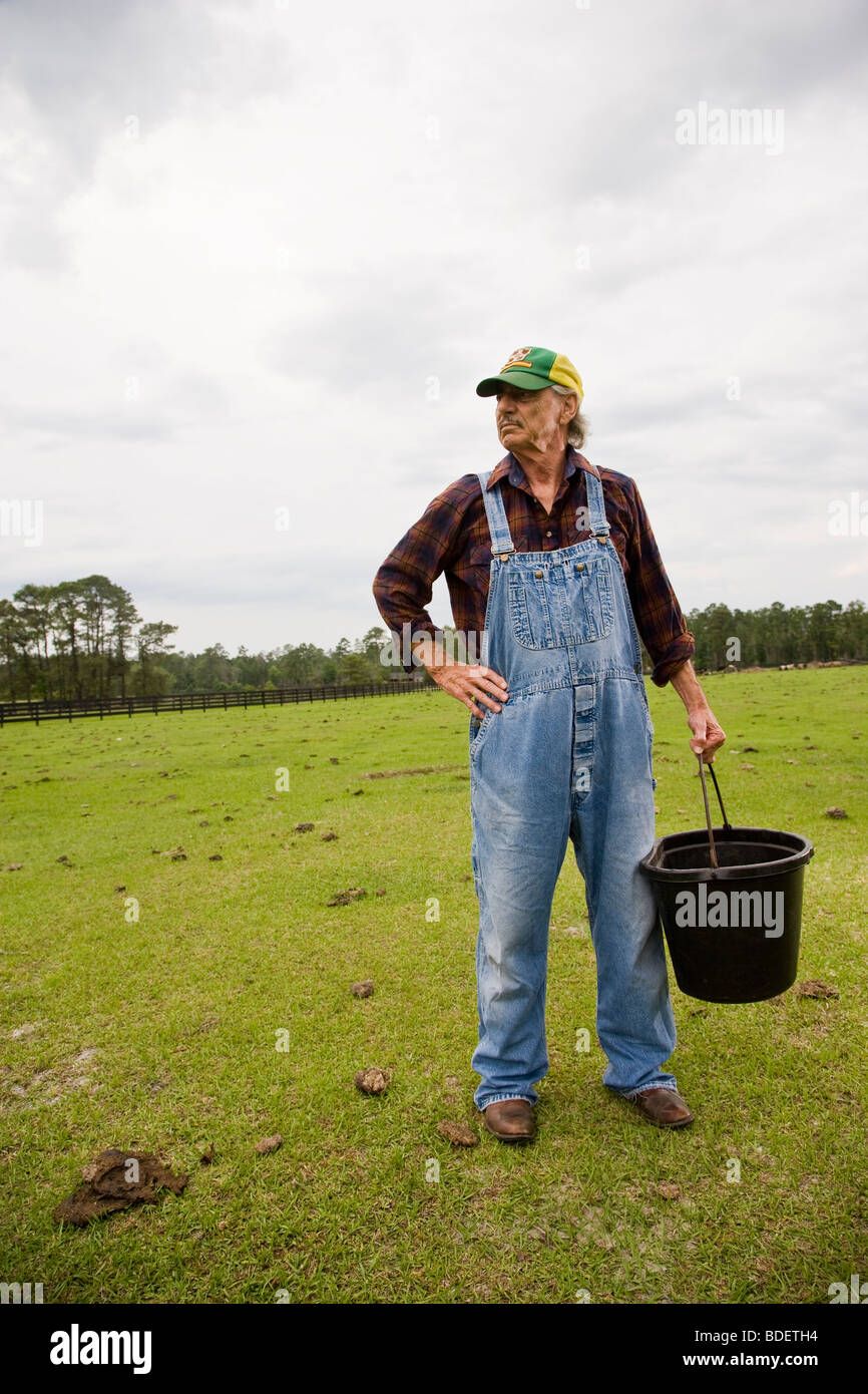 Farmhand in overalls carrying bucket in green pasture Stock Photo - Alamy