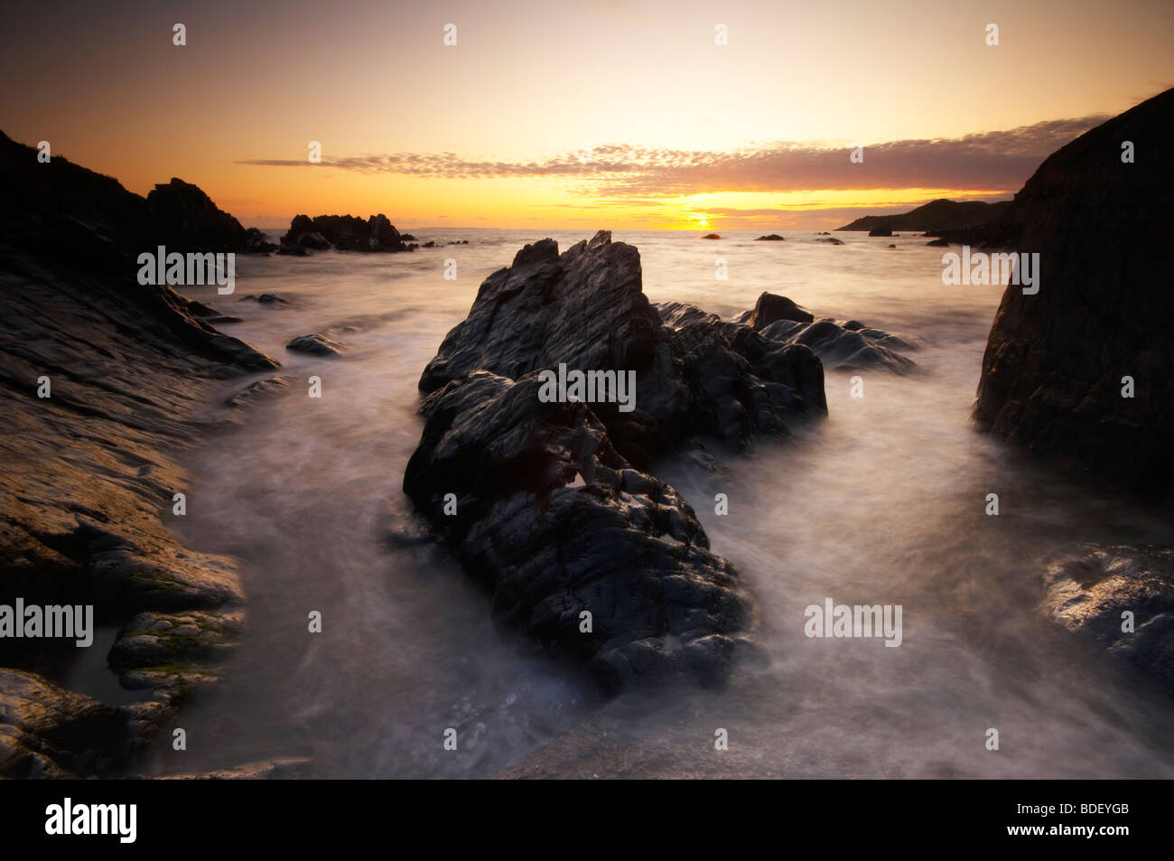Waves rushing in around foreshore rocks in Combesgate bay at sunset ...