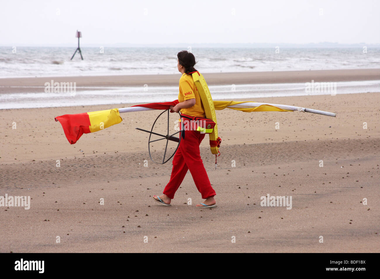 Lifeguard walking on beach with flag and equipment Stock Photo - Alamy