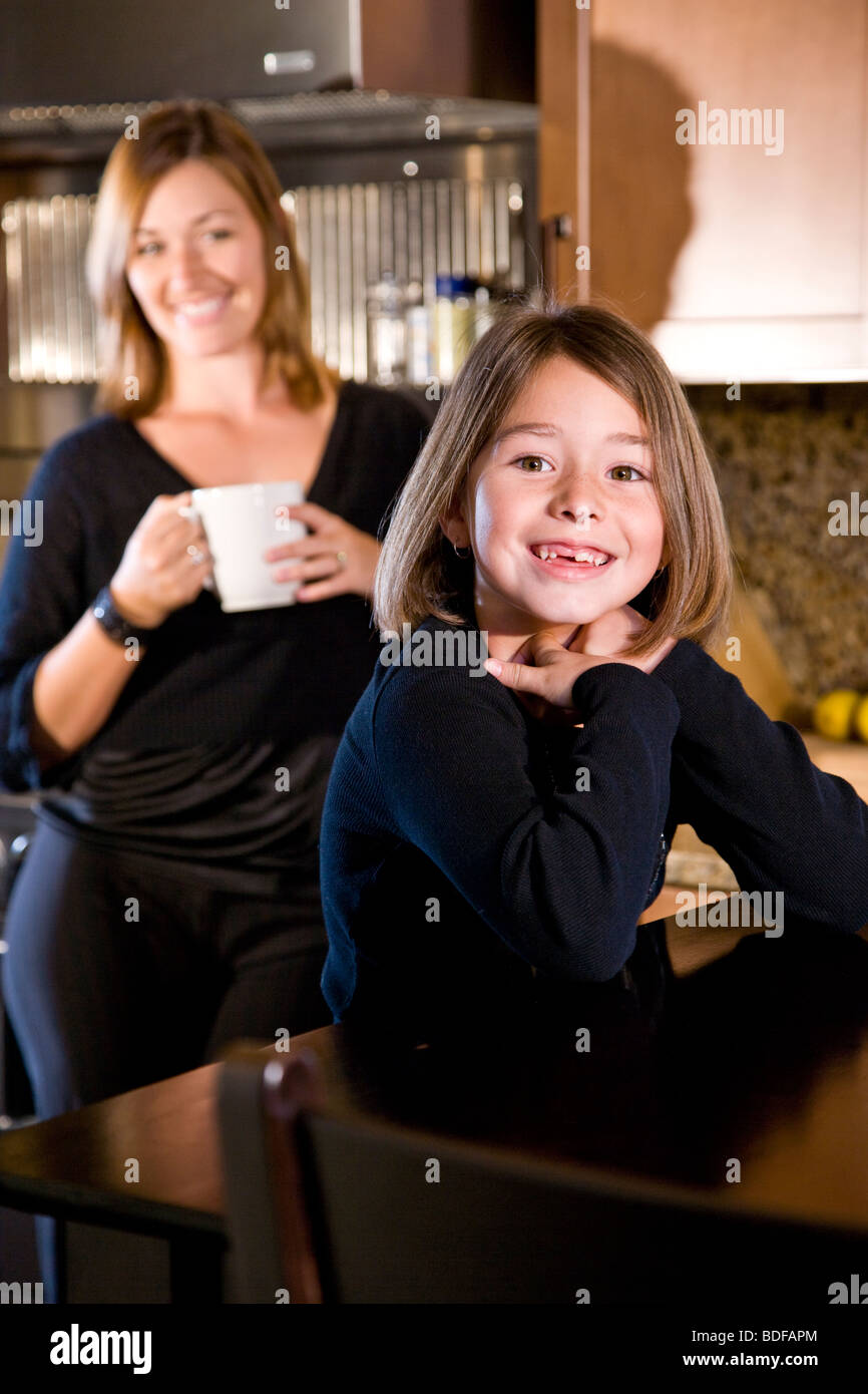 Little girl grinning with mother in background in kitchen Stock Photo ...