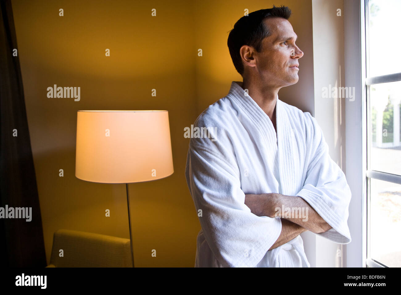Mid-adult man in robe looking out of window Stock Photo - Alamy