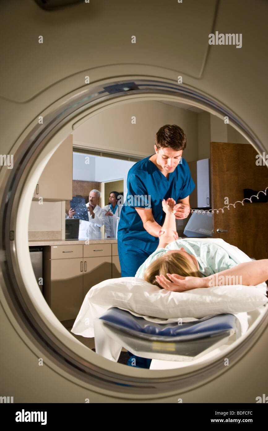Patient lying on CAT scan machine while healthcare worker takes pulse ...