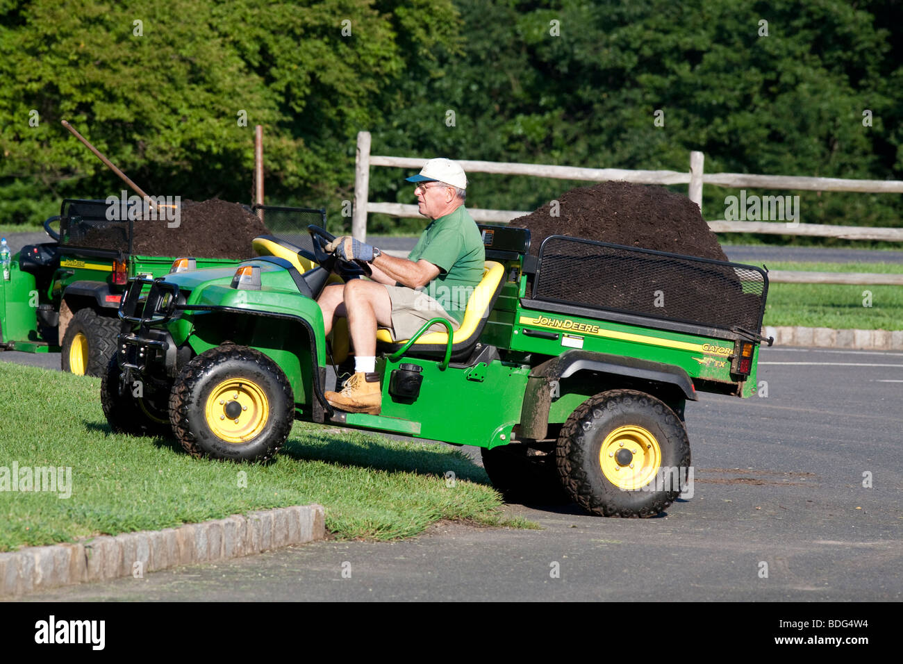 A gardener driving away with a load of mulch in the bed of a John Deere ...