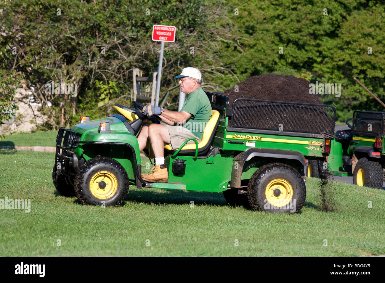 A gardener driving away with a load of mulch in the bed of a John Deere ...