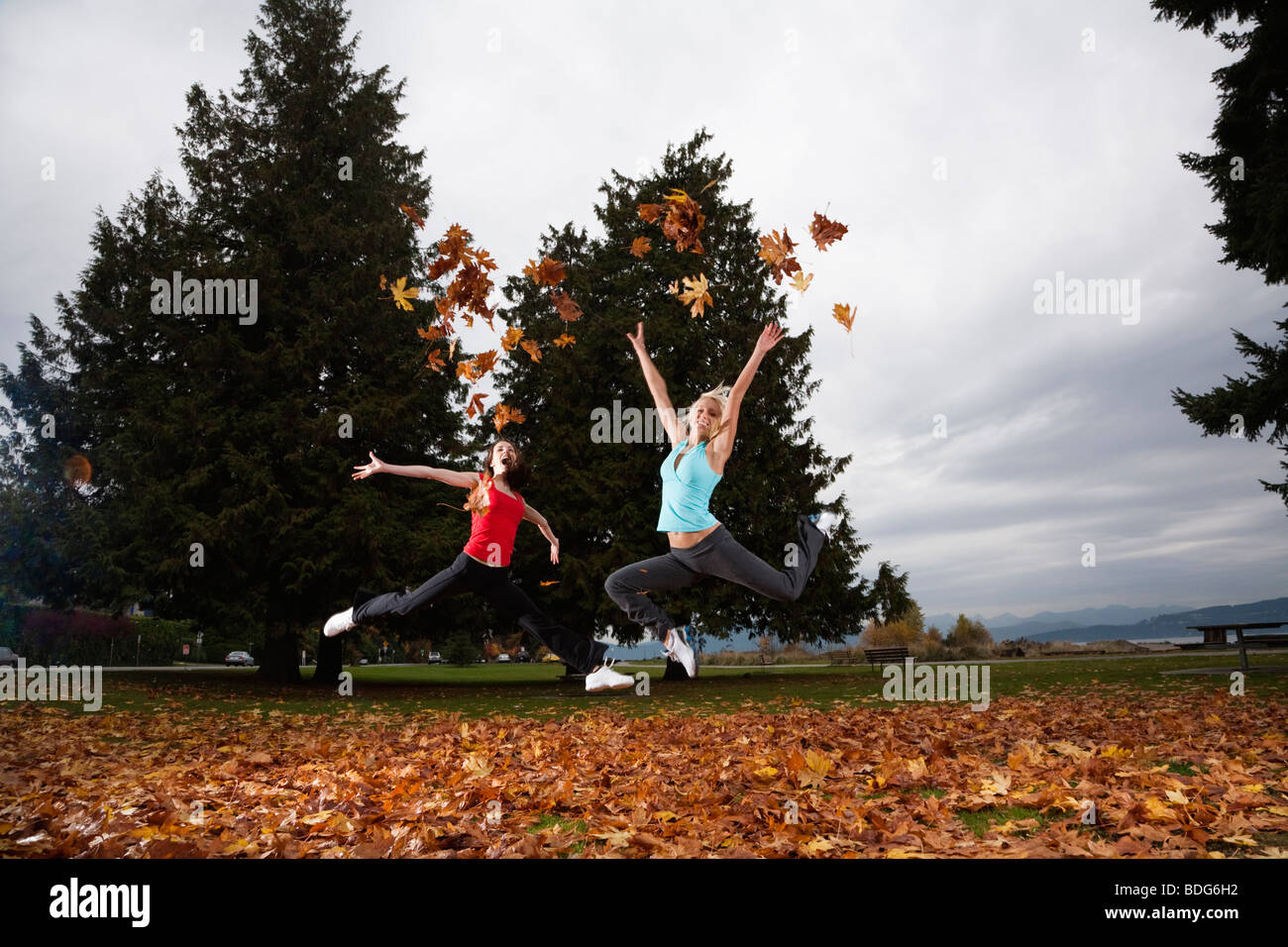Two young cheerleaders do cheers with handfuls of autumn leaves ...