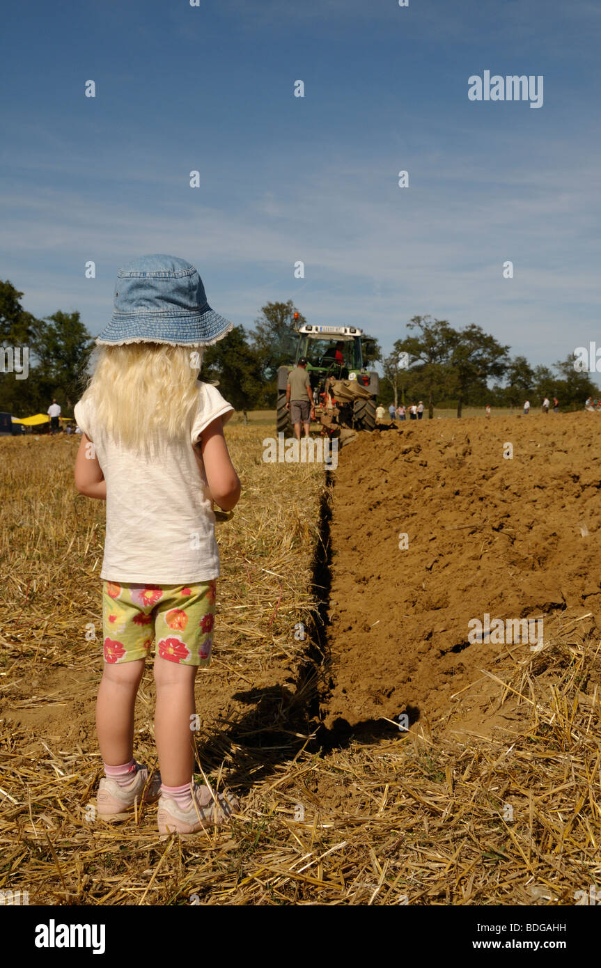 Stock photo of a little girl watching a tractor plough a field in a ...