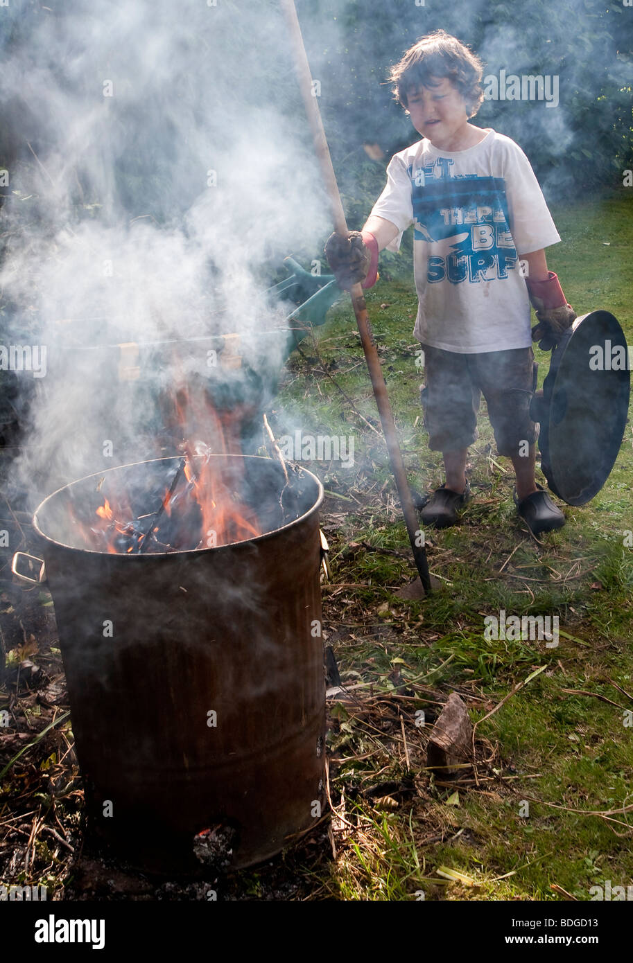 Young boy aged seven burning garden waste in incinerator with billowing ...