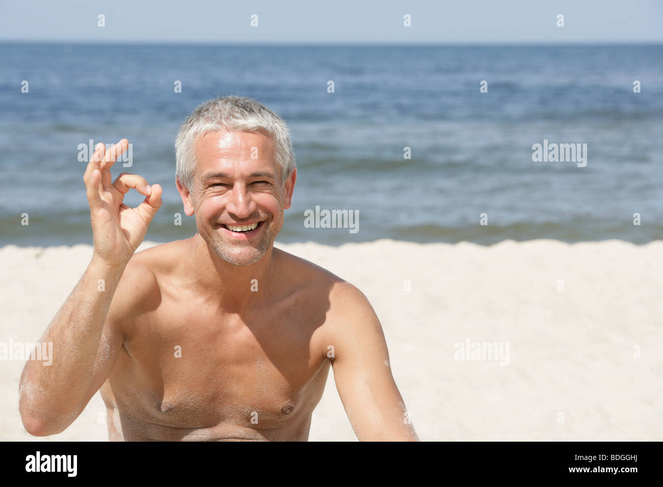 Handsome man indicating OK sign on the beach Stock Photo - Alamy