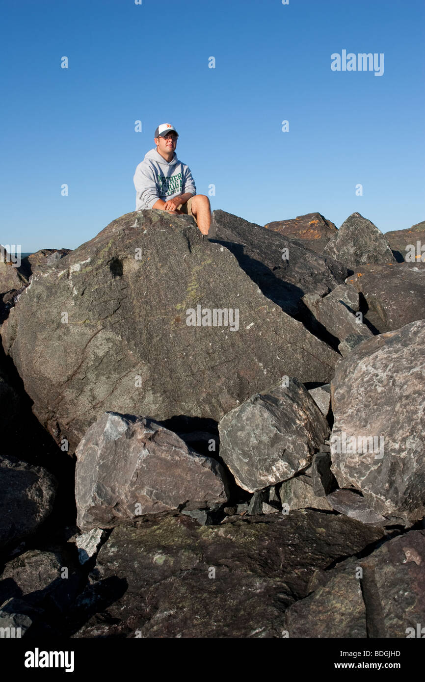 Young man sitting on large rocks against a blue sky Stock Photo - Alamy