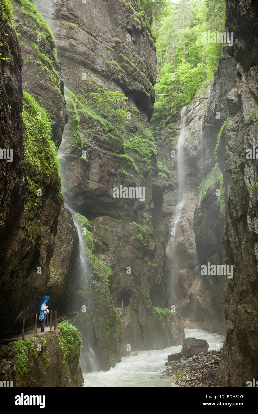 1 female tourist standing under waterfalls holding umbrella looking at ...