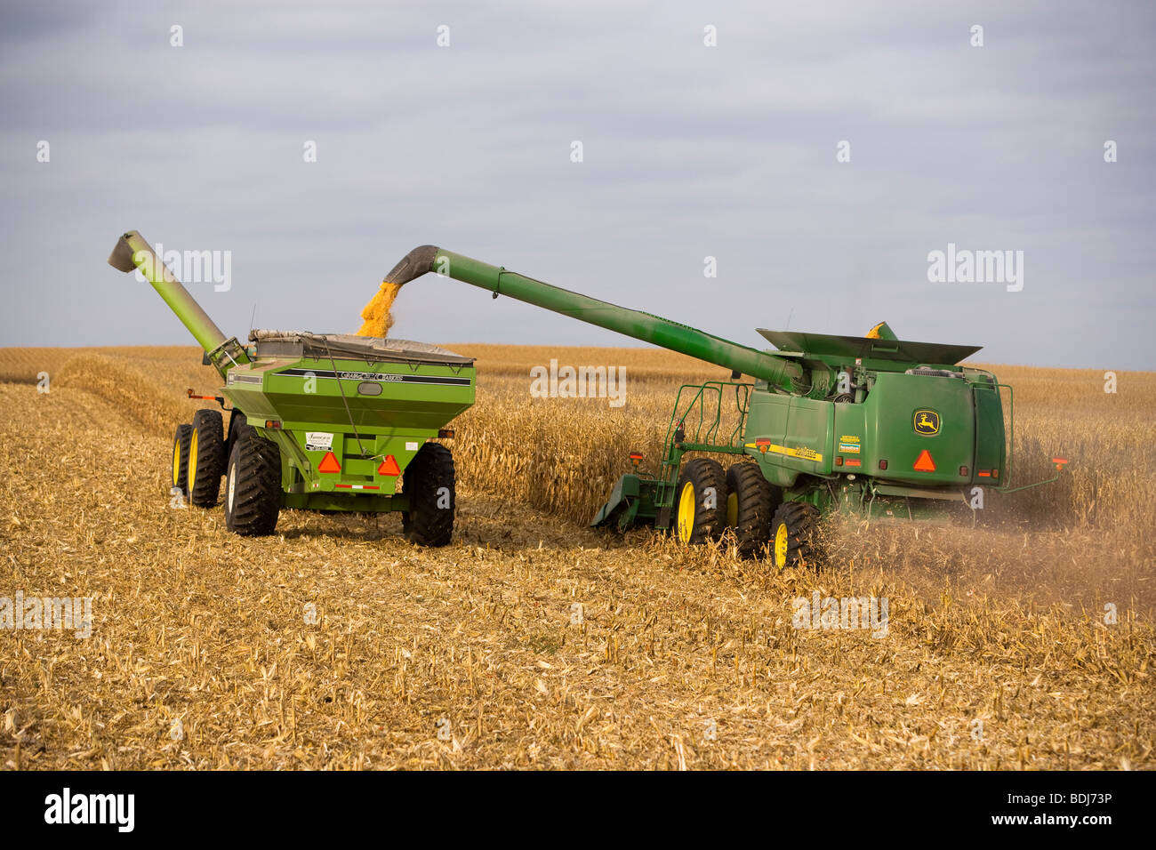 A John Deere combine harvests grain corn and unloads into a grain cart ...