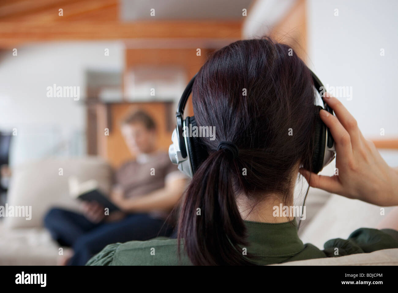 Back View of Woman Wearing Headphones, Man Reading in the Background ...