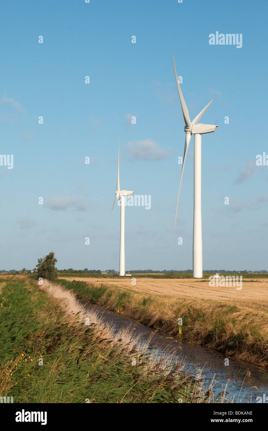 a fenland wind farm against a blue sky with a drainage channel in the ...