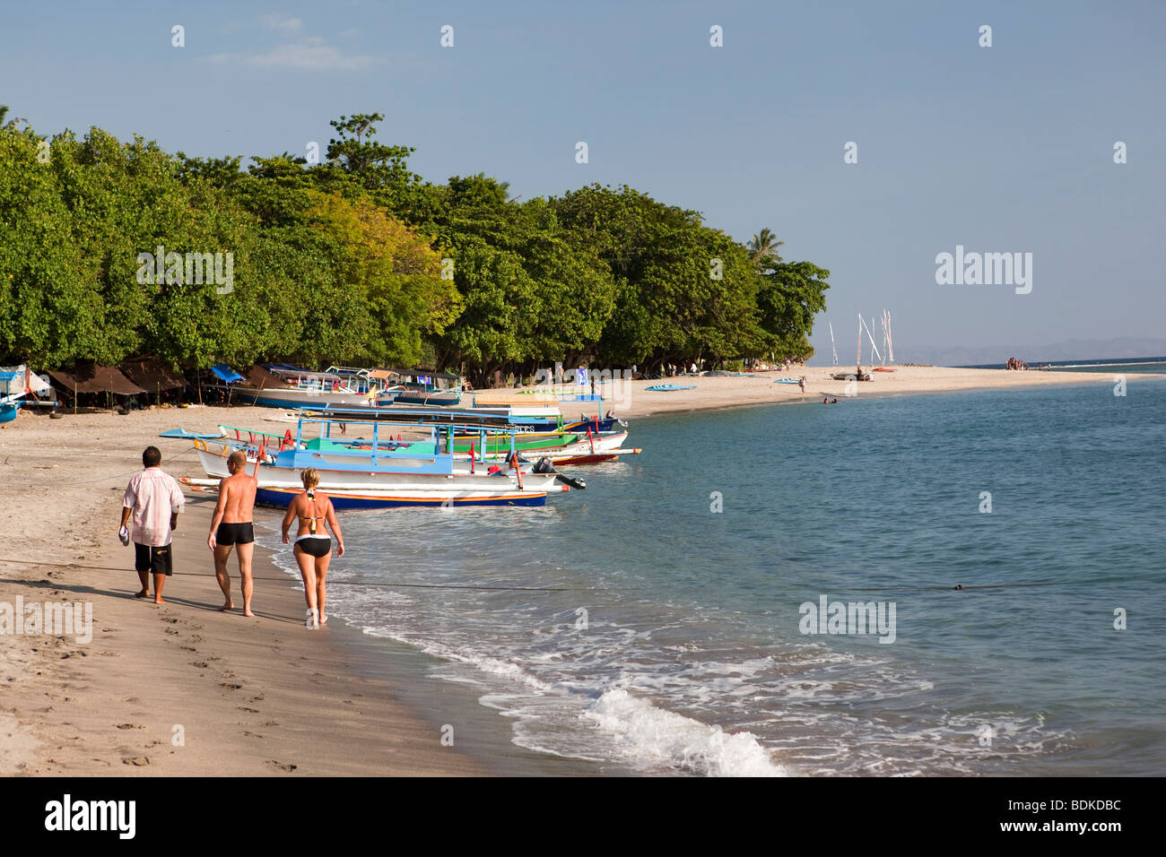 Indonesia, Lombok, Sengiggi, couple walking colourful outrigger fishing ...