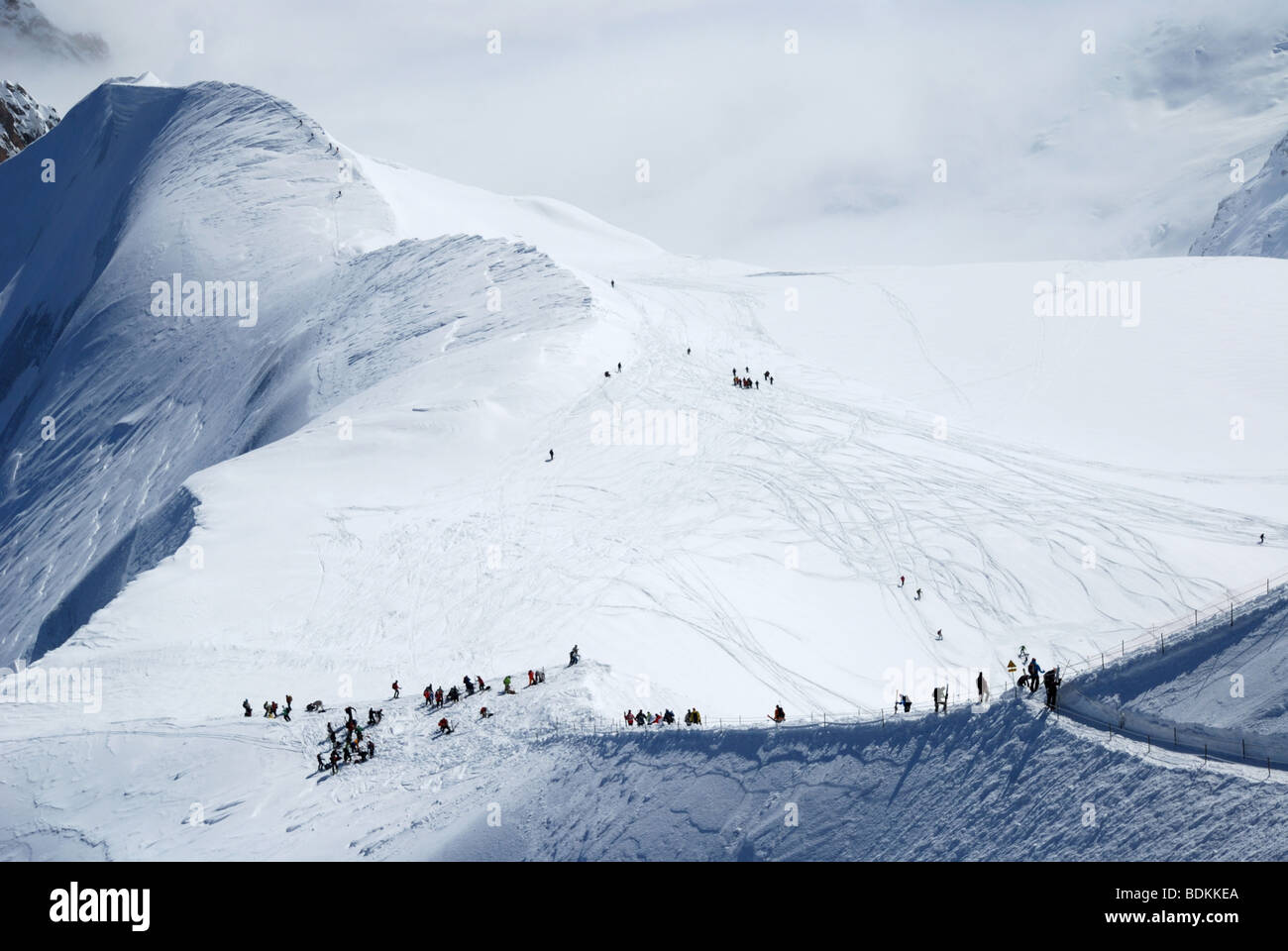 White slope with many black figures of mountain-skiers against clouds ...
