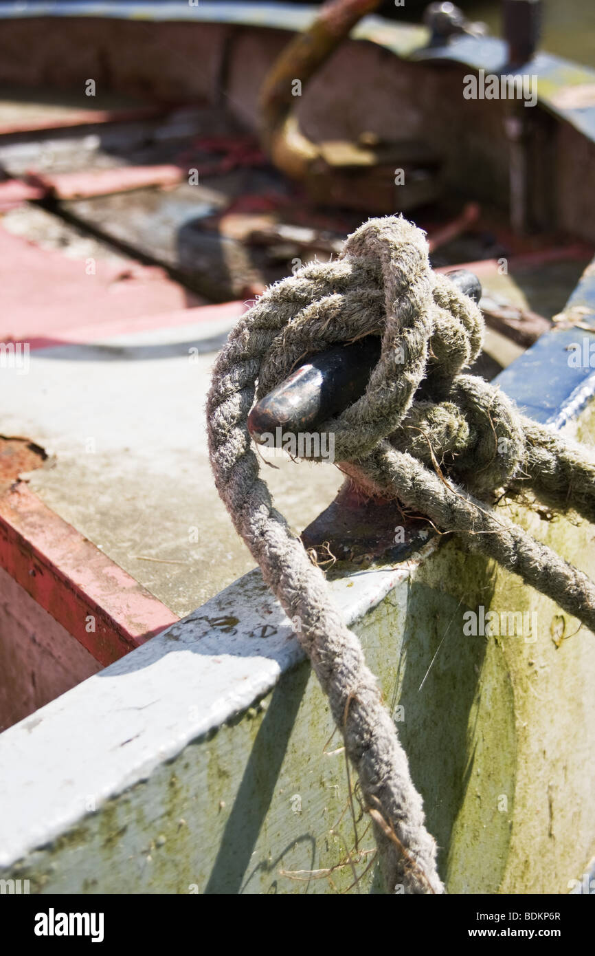 A worn piece of rope, tied to an old narrow boat with peeling paint ...