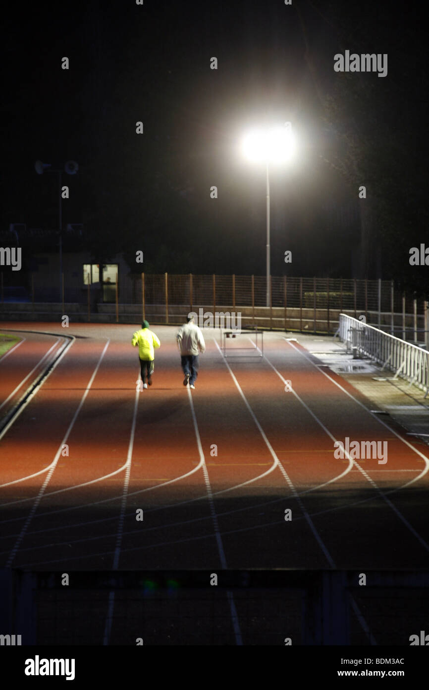 two men running on athletic track at night Stock Photo - Alamy