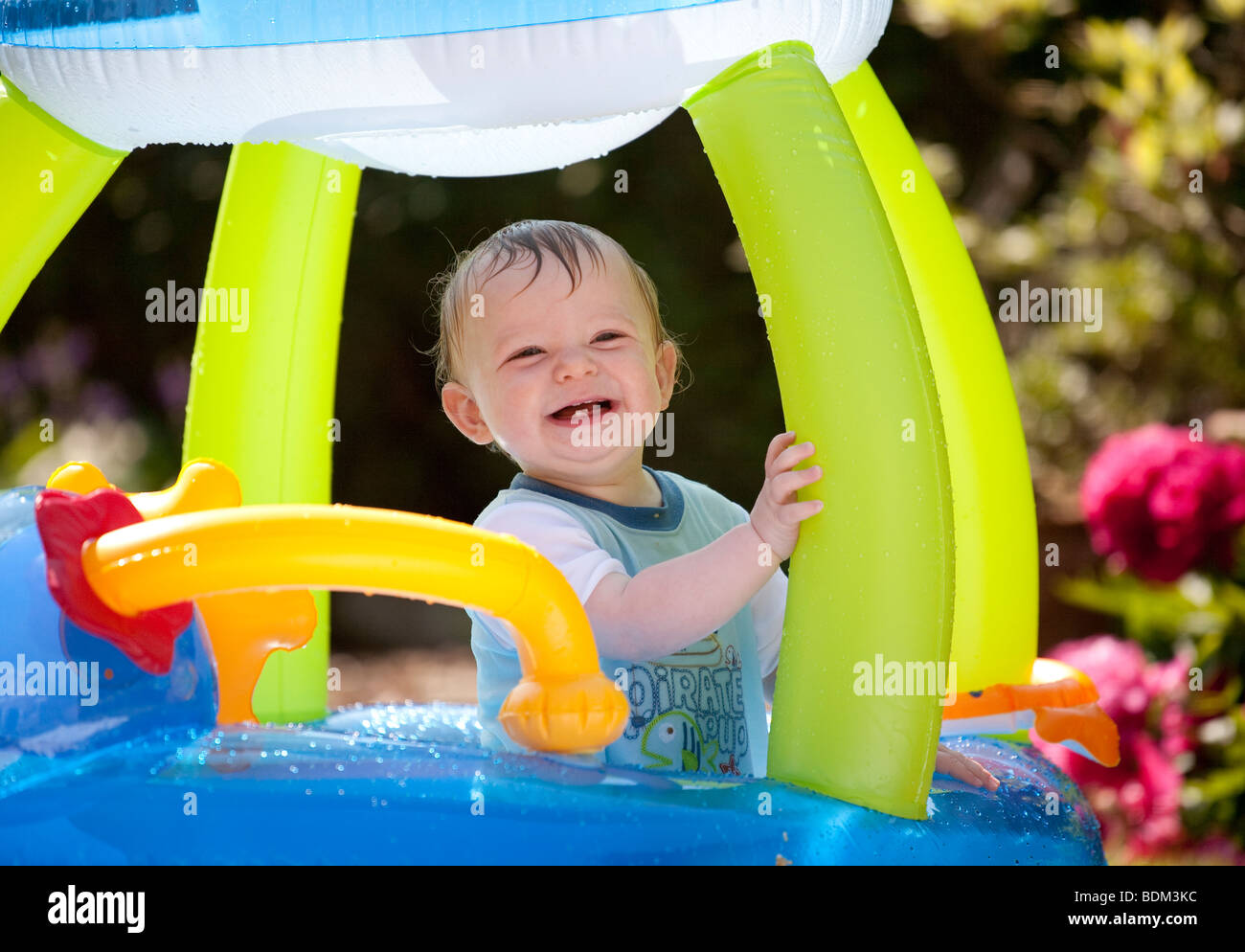 A baby boy playing in an inflated plastic boat paddling pool on a ...