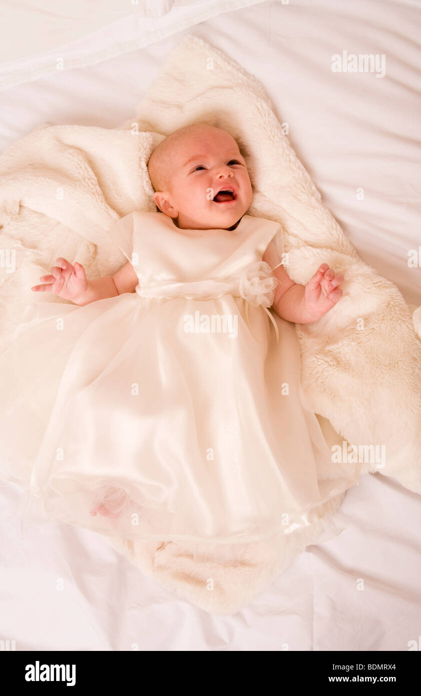 Two-month-old baby girl wearing a white silk dress, lying on a soft ...