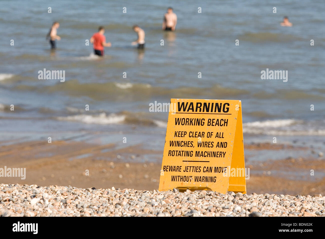 Warning sign on the beach while people swim Stock Photo - Alamy