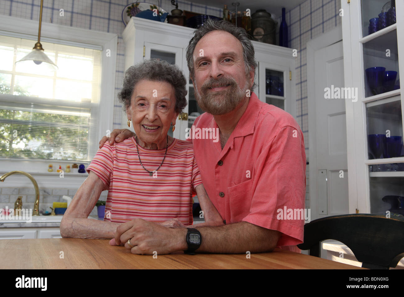 Elderly mother and her gay son caretaker in the kitchen of their home ...