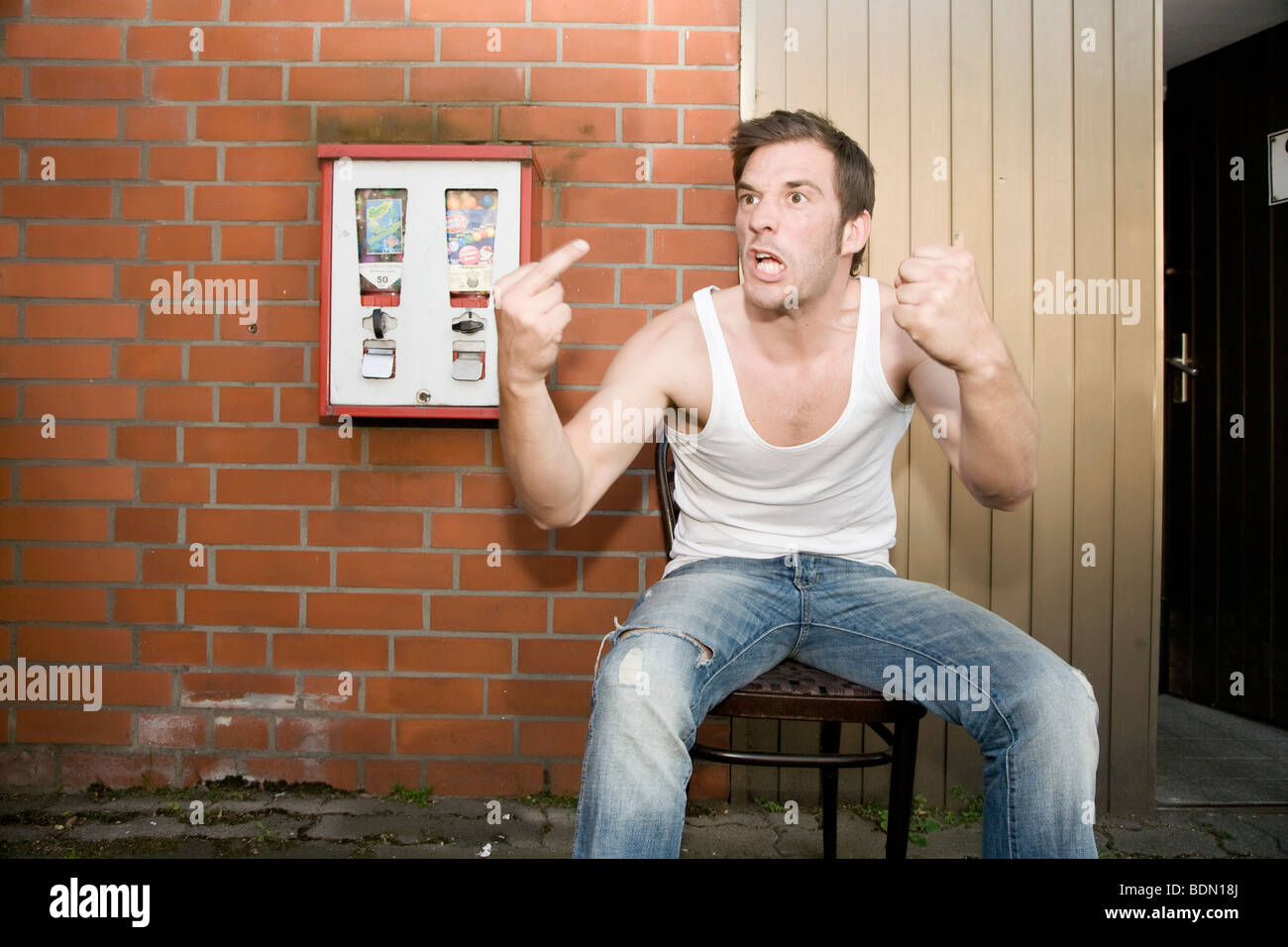 Young man, rowdy sitting and gesturing provocatively in front of a ...
