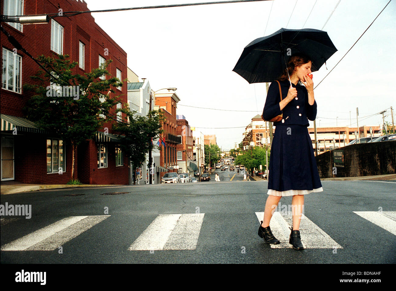 A young lady crossing the road on a zebra crossing holding an umbrella ...
