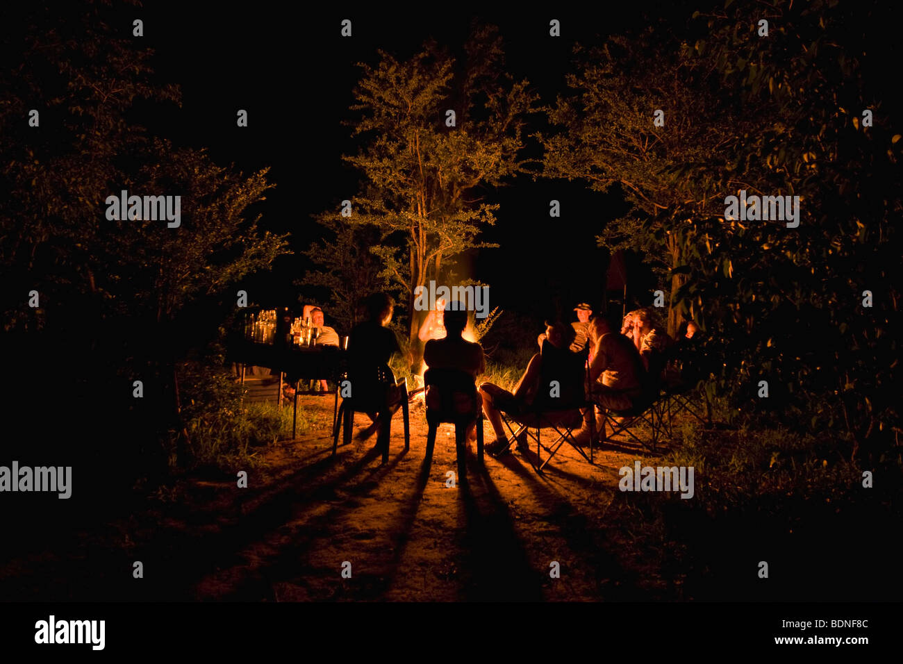 People gathered around campfire, Vakani Camp, Hwange National Park ...