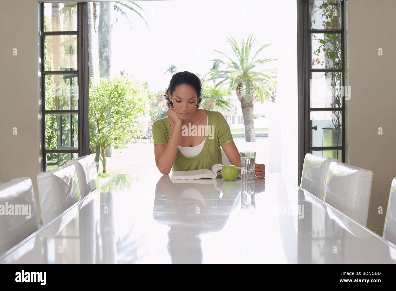 Woman reading book, sitting at dining table Stock Photo - Alamy