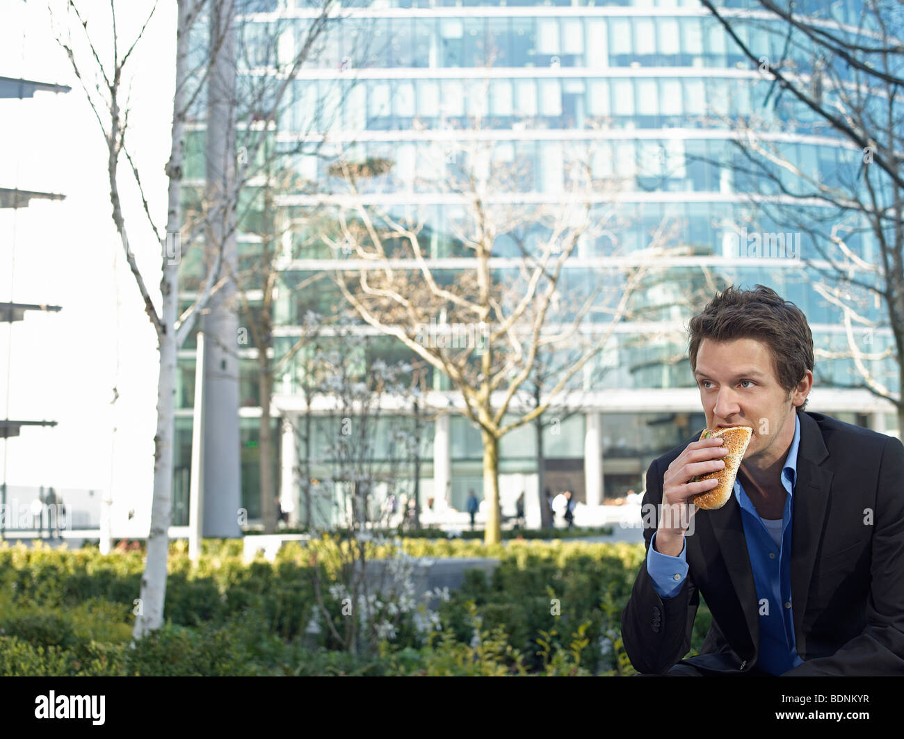 Mid adult businessman sitting in front of office building, eating ...