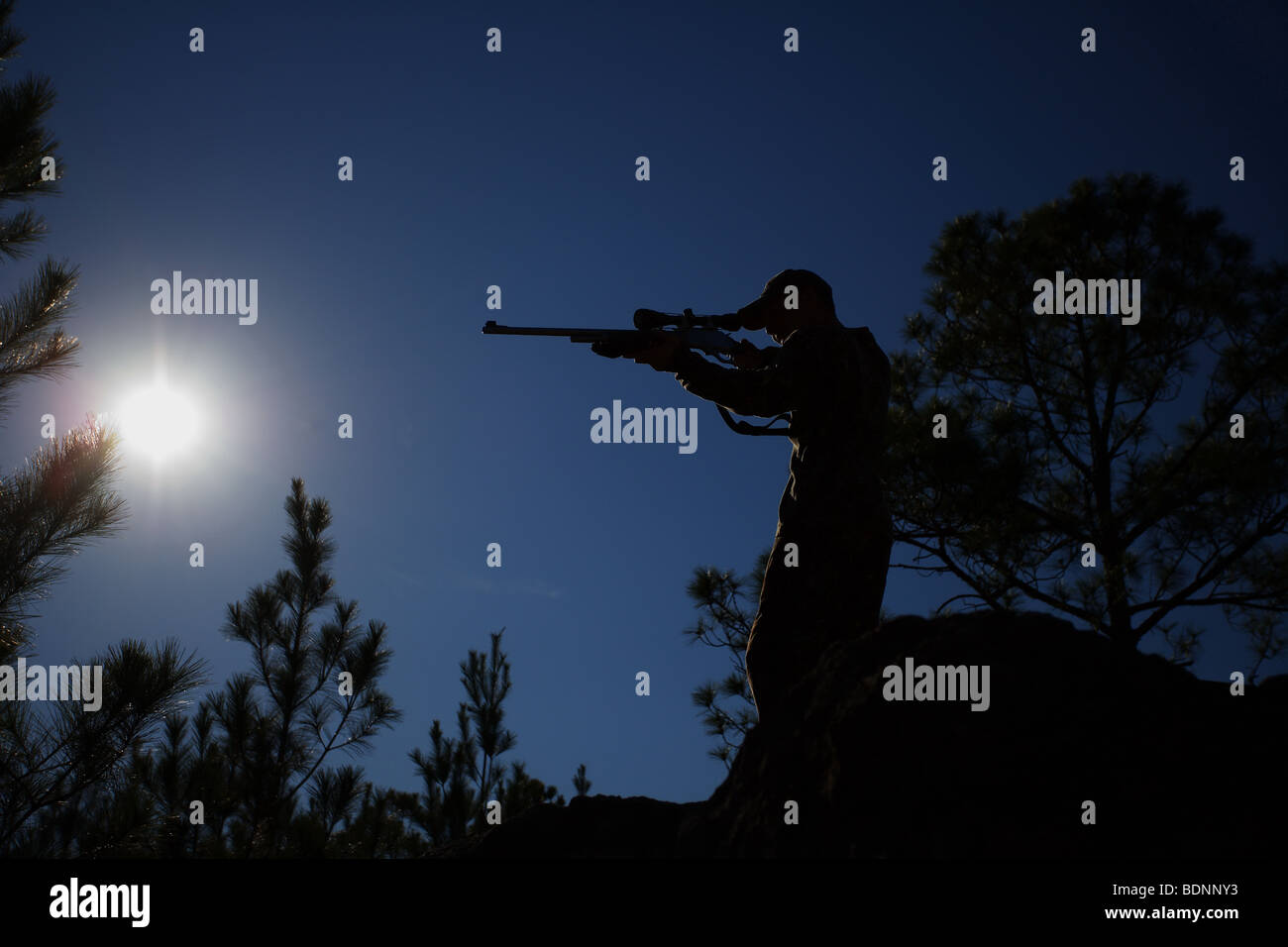 SILHOUETTE VIEW HUNTER STANDING ON ROCKY CLIFF FIRING WEAPON PINE ...